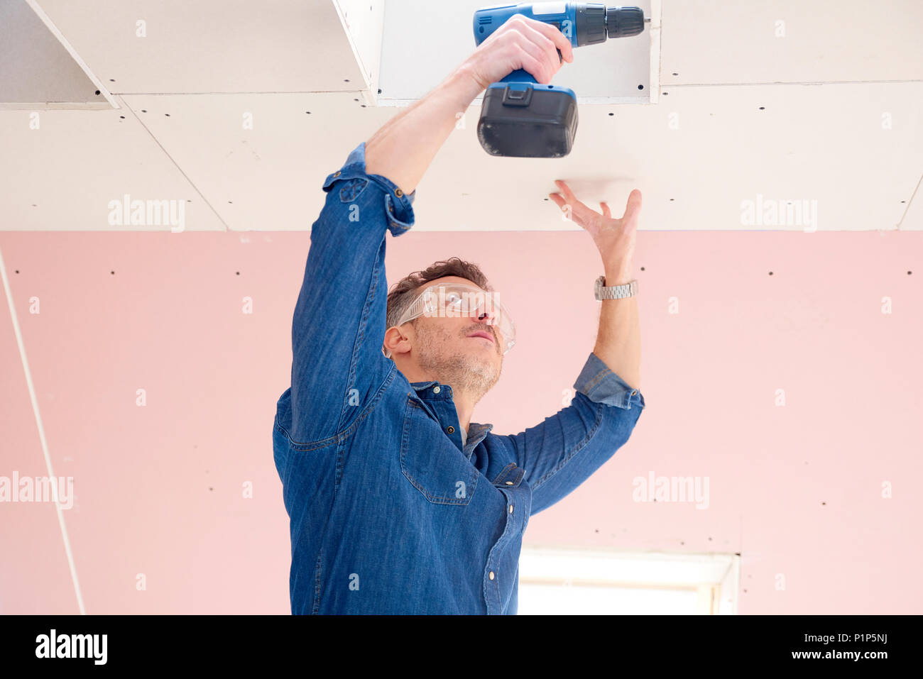 Handyman using cordless drill while working on construction site Stock ...