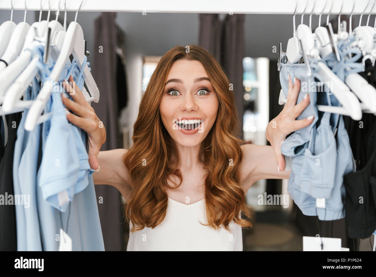 Happy young woman standing at the clothing rack Stock Photo - Alamy