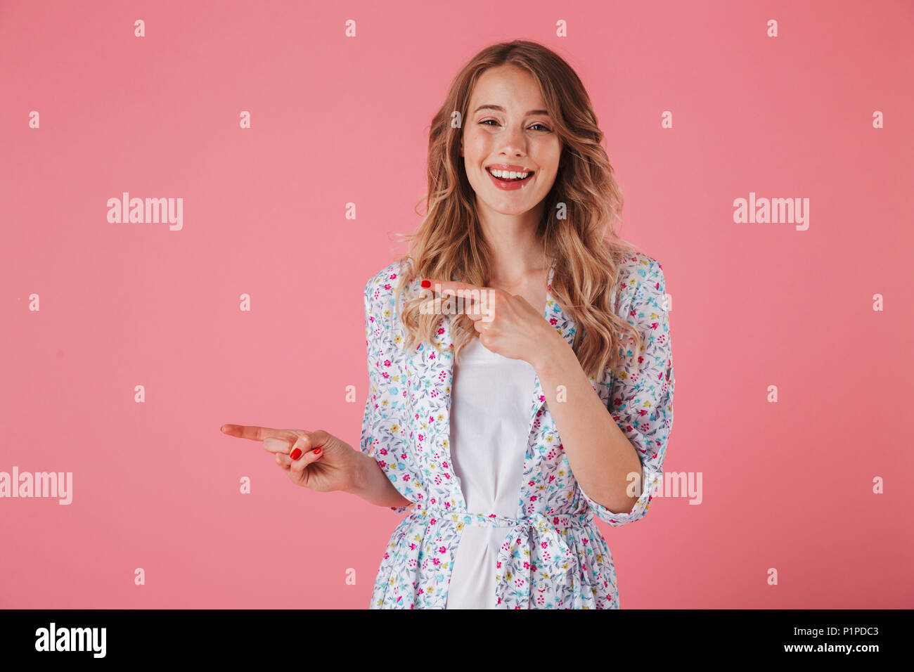 Portrait of an excited young woman in summer dress pointing finger ...