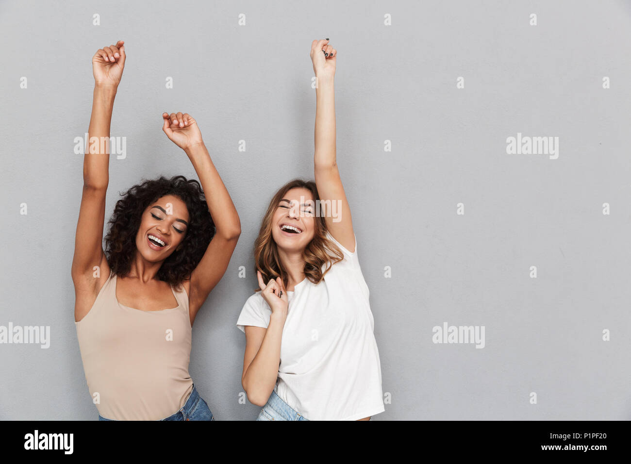 Portrait of two happy young women dancing and having fun isolated over ...