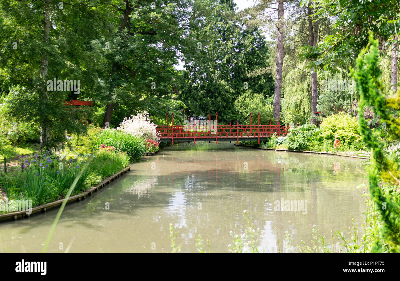 A red ornamental bridge spans over a large pond Stock Photo - Alamy