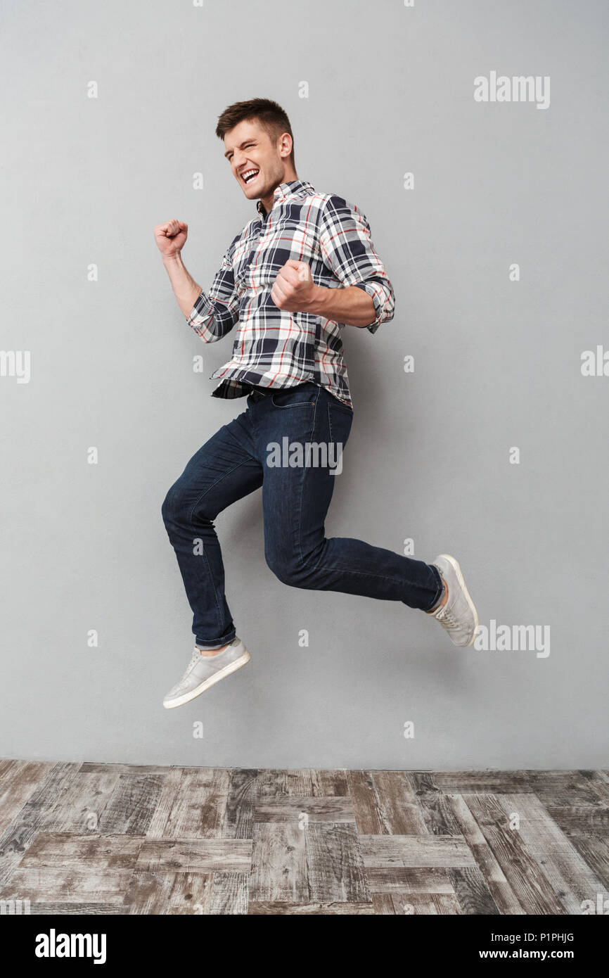 Full length portrait of a cheerful young man jumping over gray ...