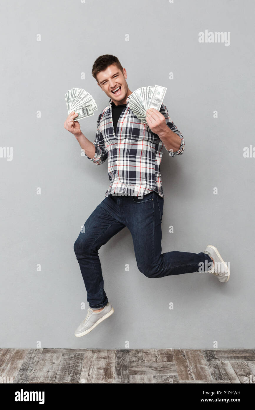 Full length portrait of a happy young man showing money banknotes while ...
