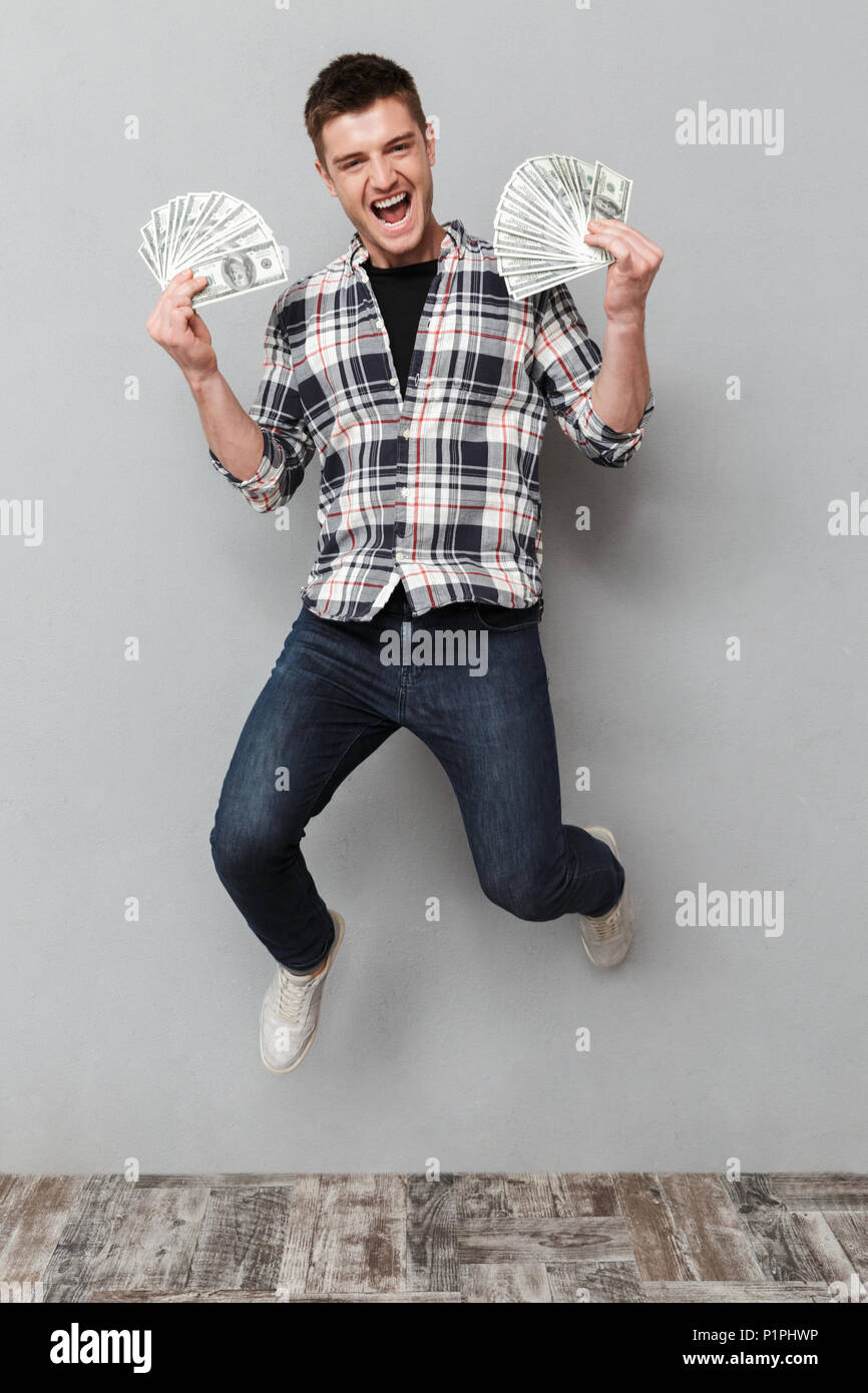 Full length portrait of a cheerful young man showing money banknotes ...