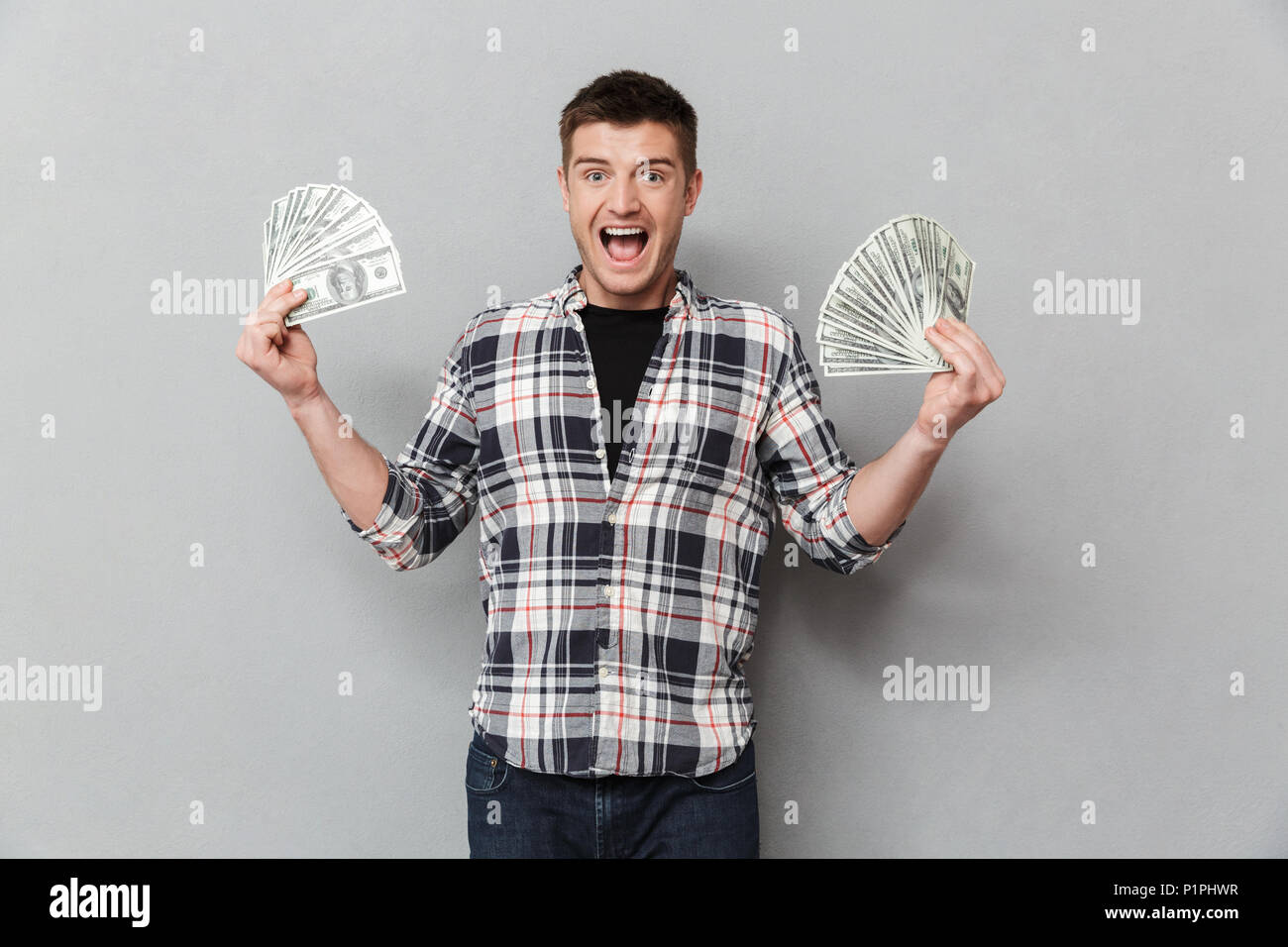 Portrait of an excited young man showing money banknotes over gray ...