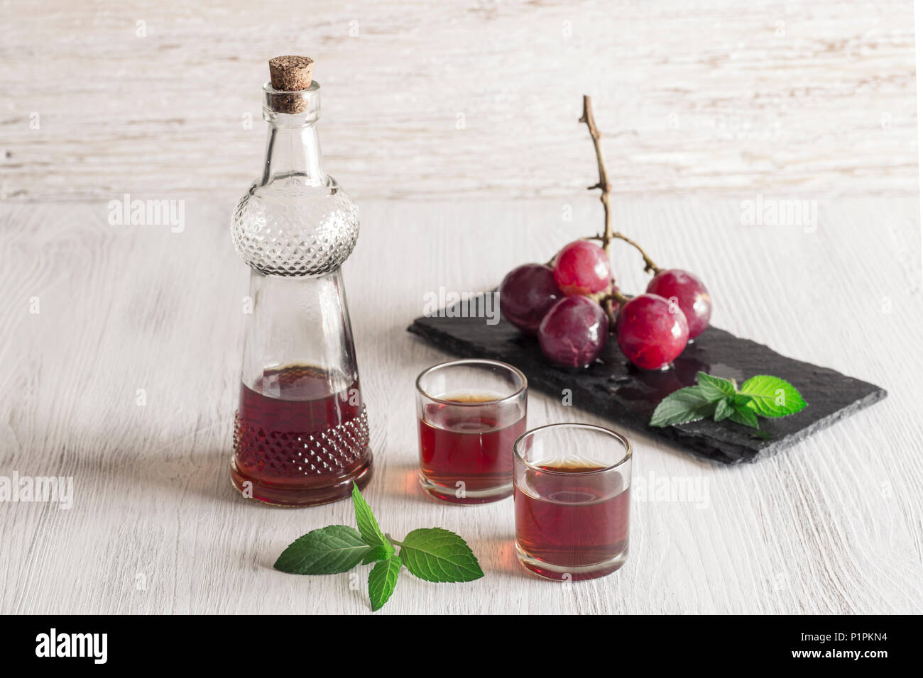 Grape liqueur in small glasses, grapes on slate table and white wood ...