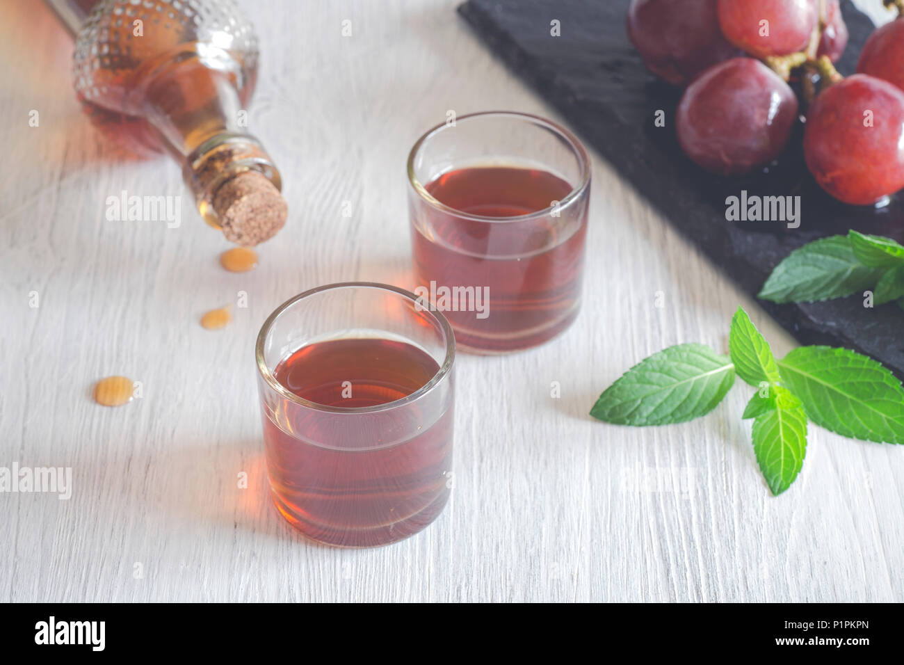 Grape liqueur in small glasses, grapes on slate table and white wood ...