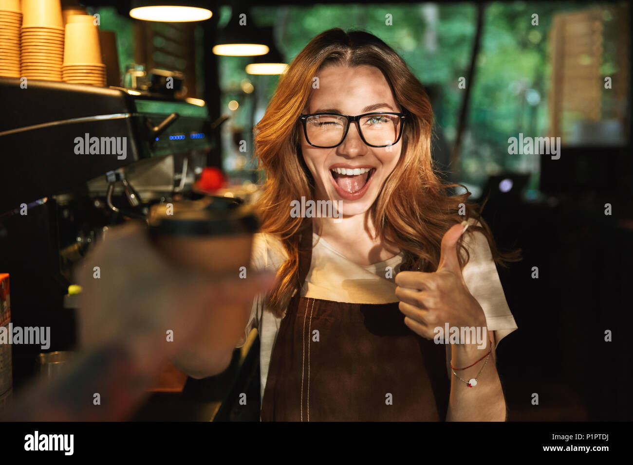 Portrait of a happy young barista girl in apron standing behind the bar ...
