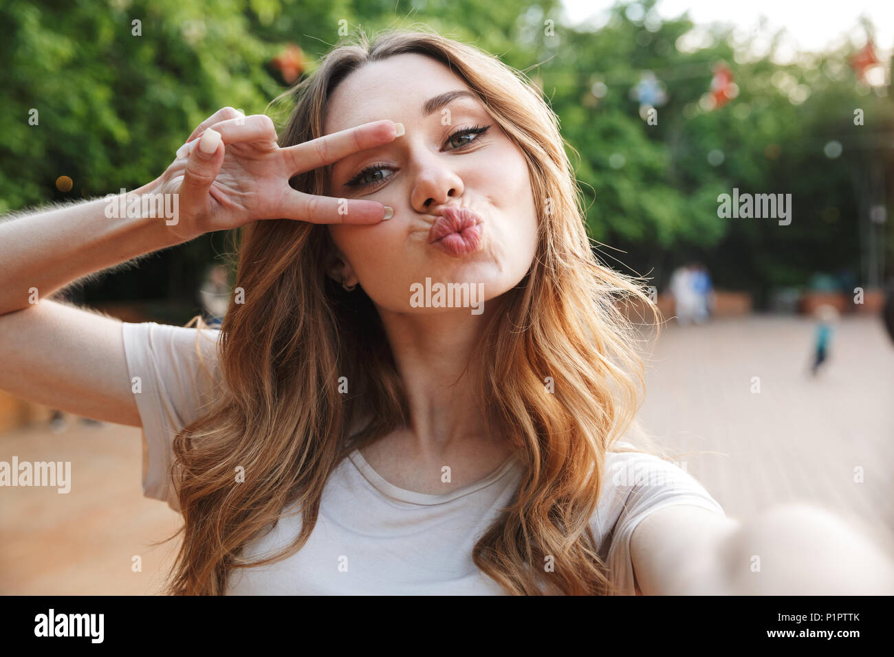 Close up of a pretty young girl taking selfie with outstretched hand outdoors and showing peace ...