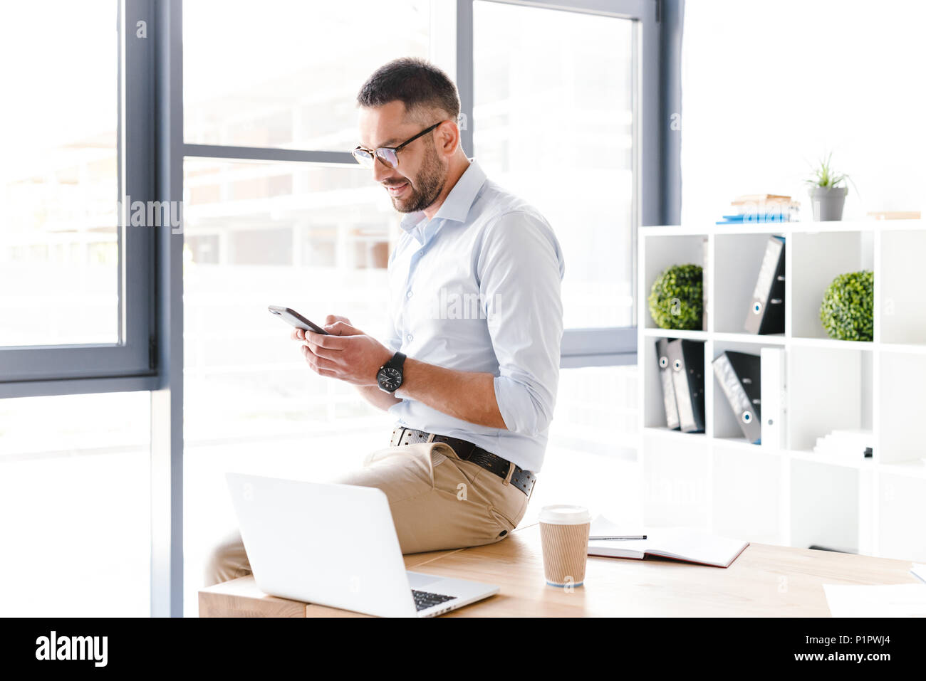 Image of adult handsome man in formal wear sitting on table in office ...