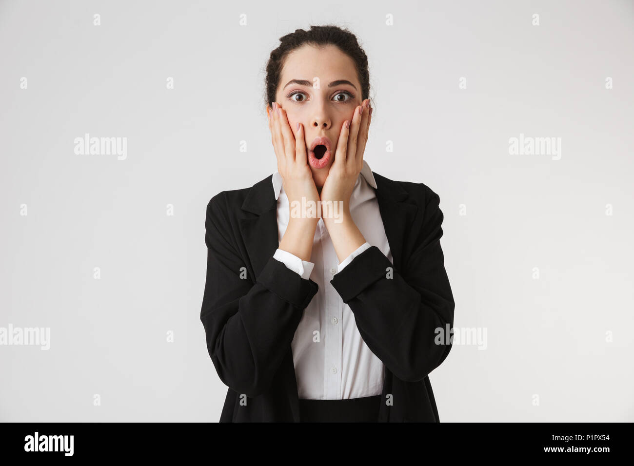 Portrait of a shocked young businesswoman holding arms at her face ...