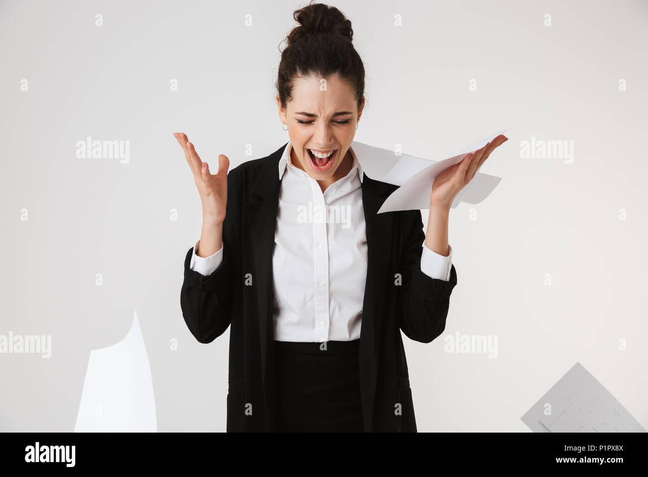 Portrait of an angry young businesswoman screaming and throwing papers ...