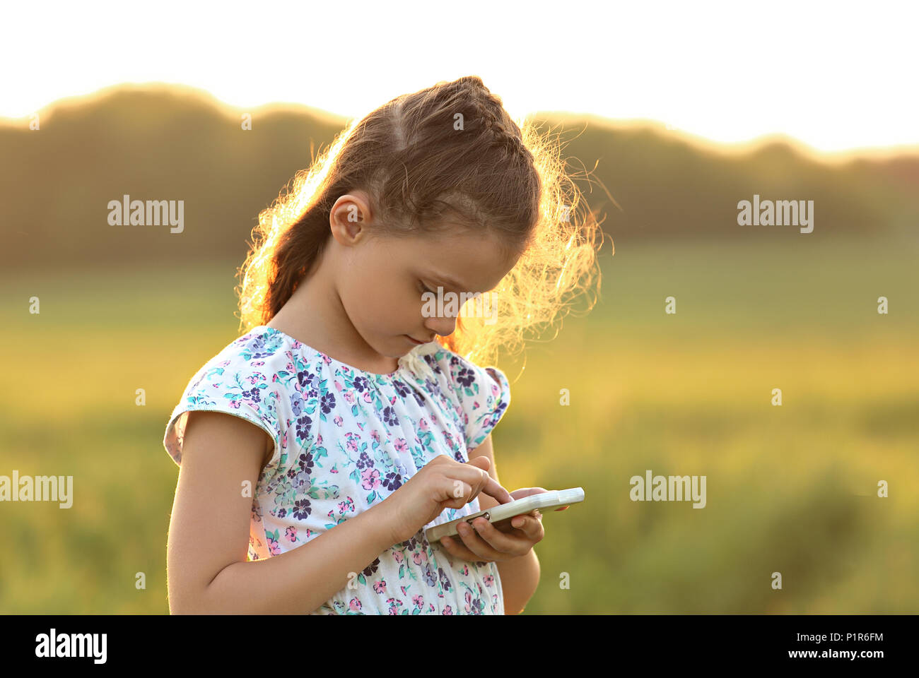 Cute kid girl texting sms on mobile phone with serious face on summer ...