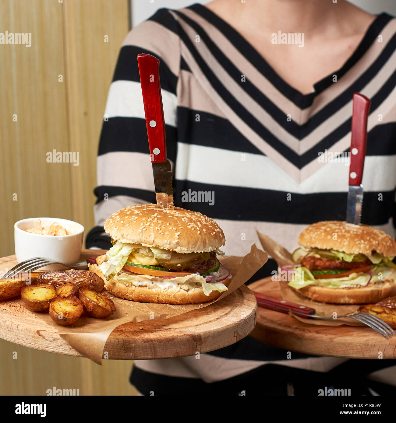 Waitress dressed in striped jumper serving pair of round wooden trays ...