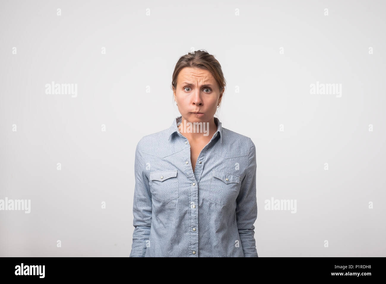 Indoor shot of cute woman in denim shirt in denim shirt having doubtful ...