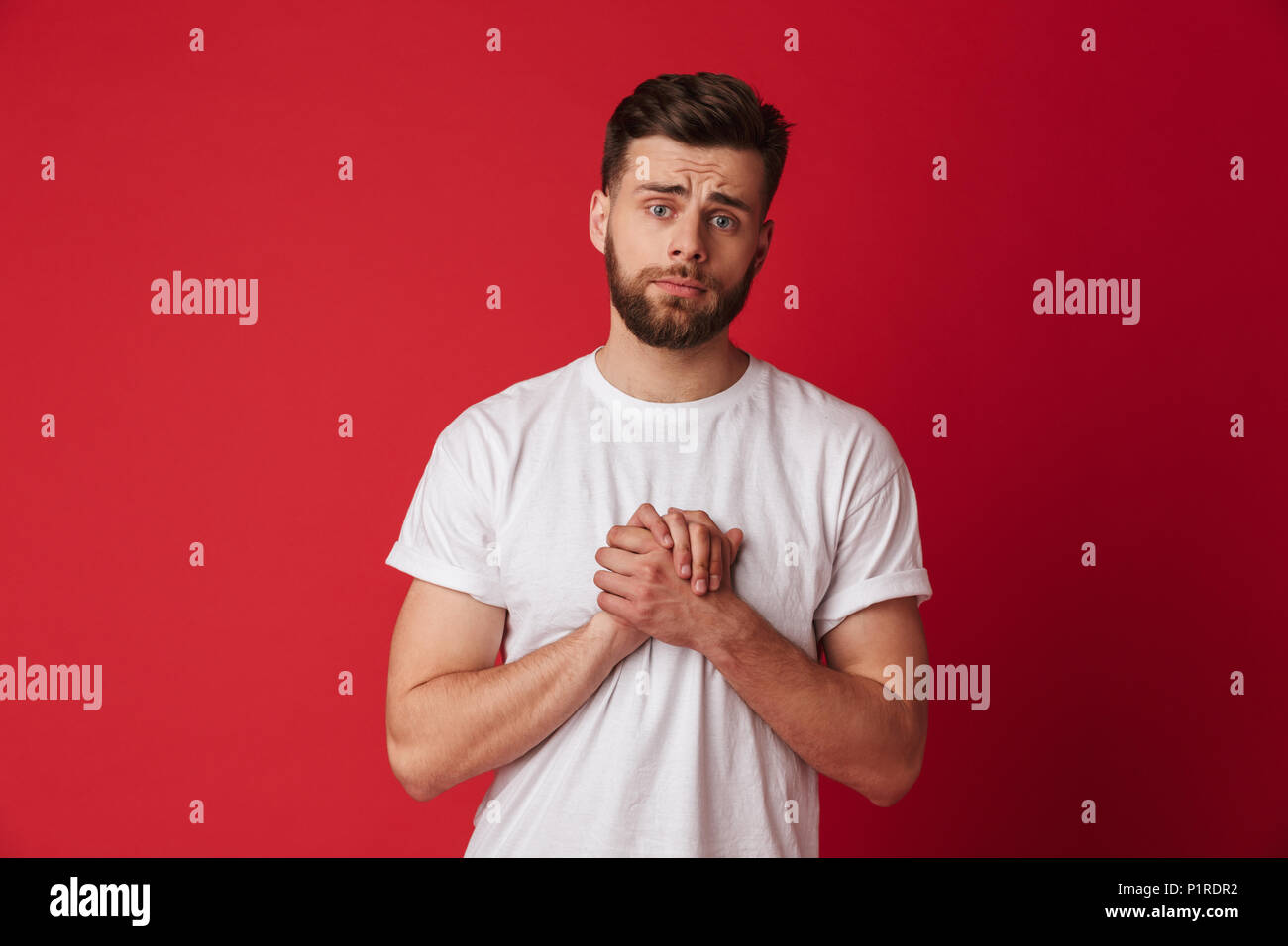 Picture of hopeful young man standing isolated over red wall background ...