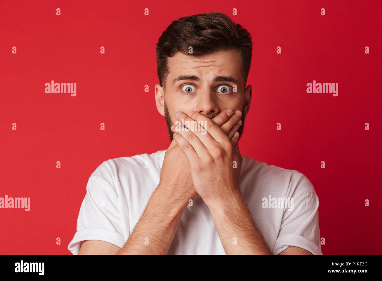 Image of scared young man covering mouth with hands standing isolated ...