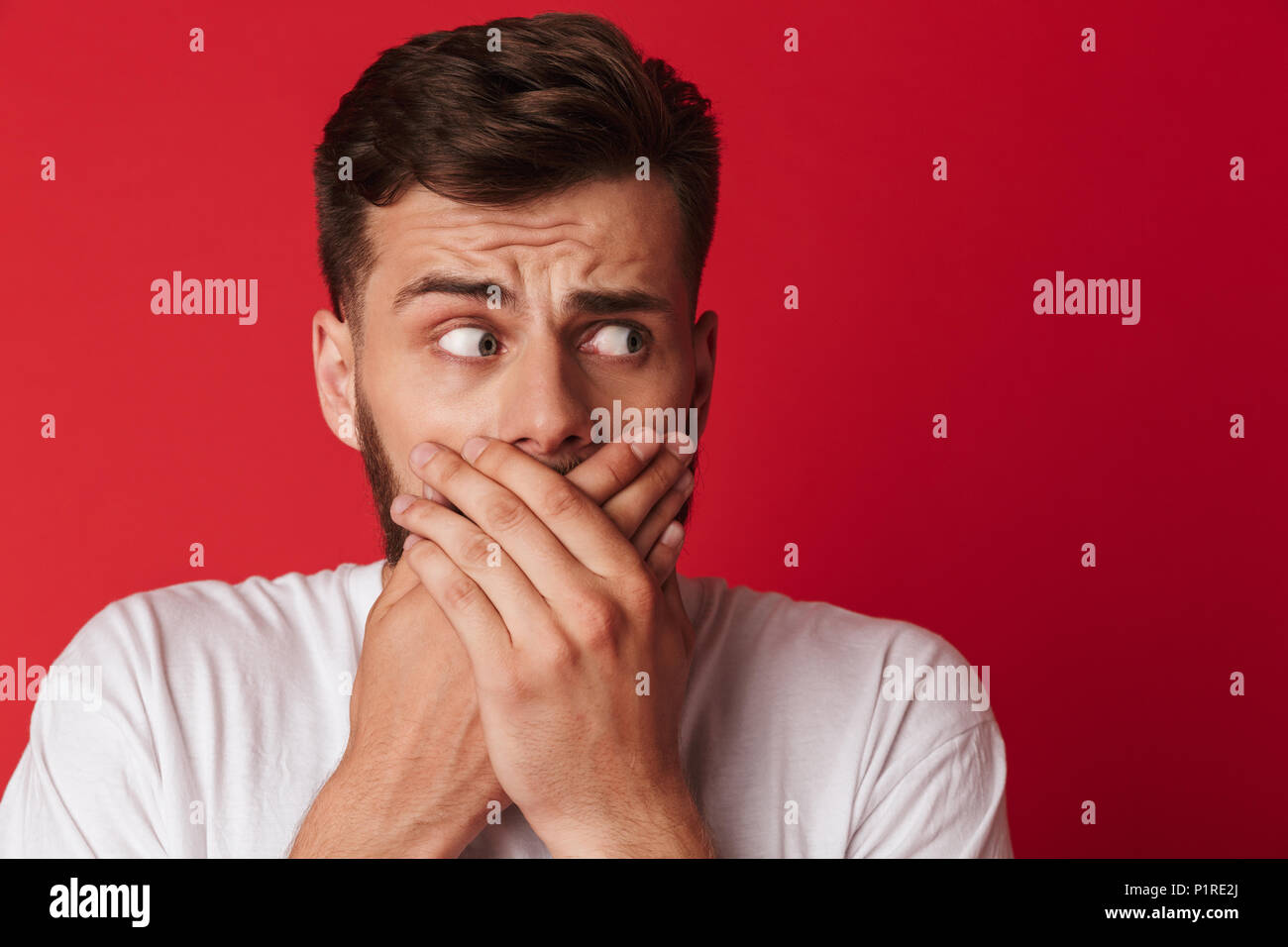 Image of scared young man covering mouth with hands standing isolated ...