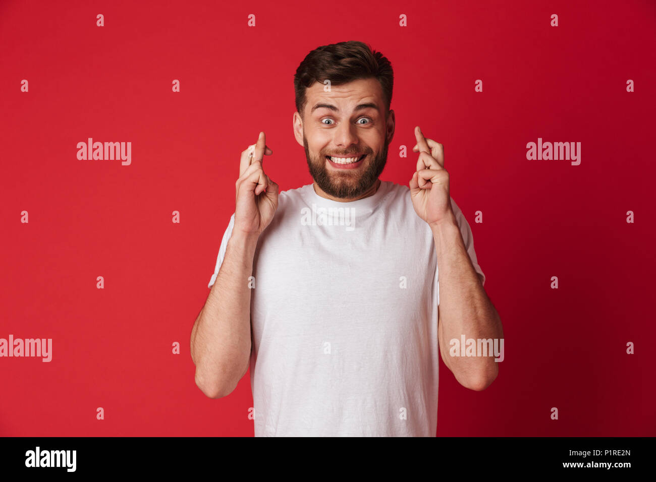 Picture of hopeful young man standing isolated over red wall background ...