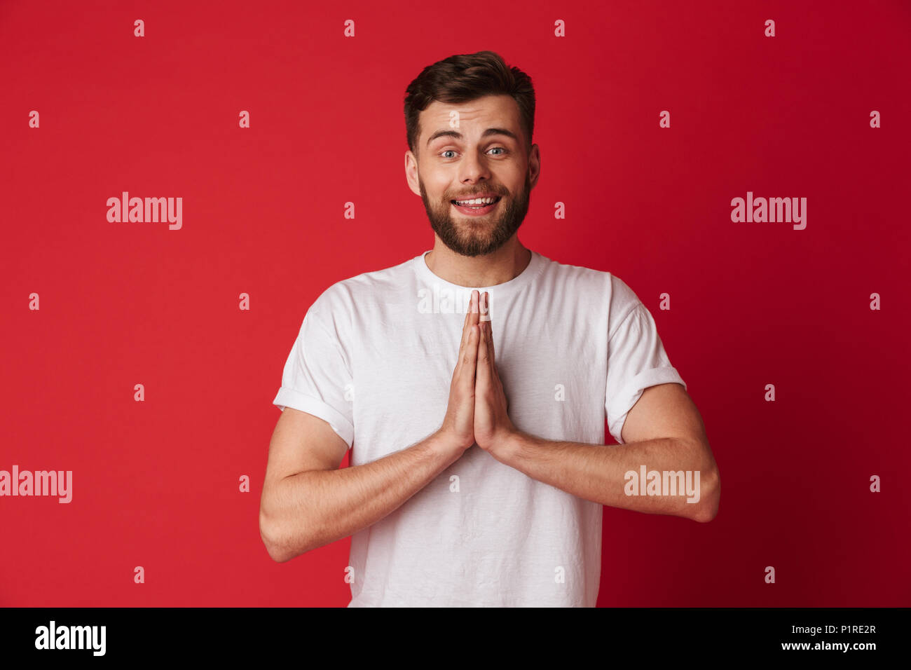 Picture of hopeful young man standing isolated over red wall background ...