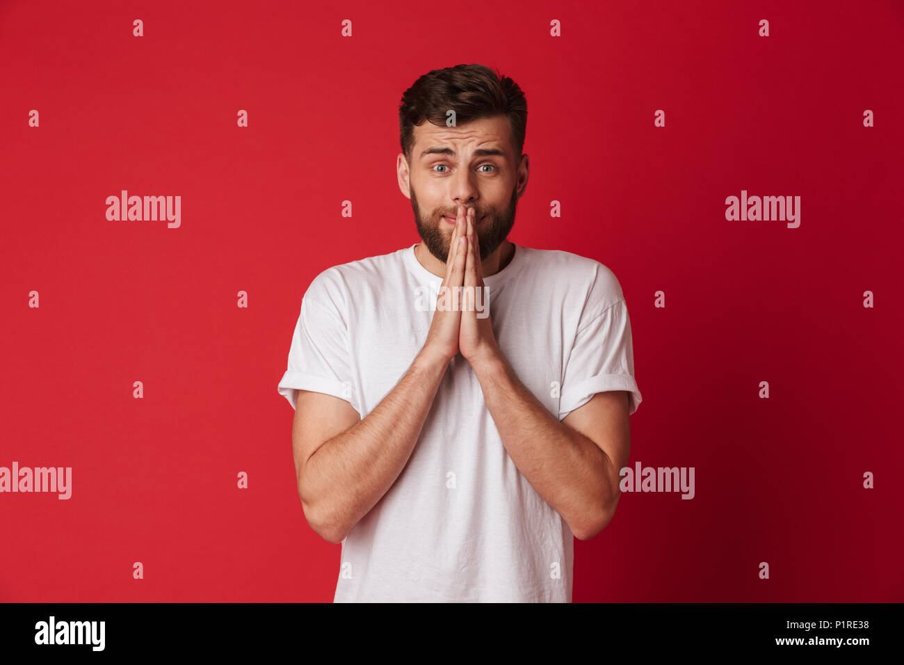 Picture of hopeful young man standing isolated over red wall background ...