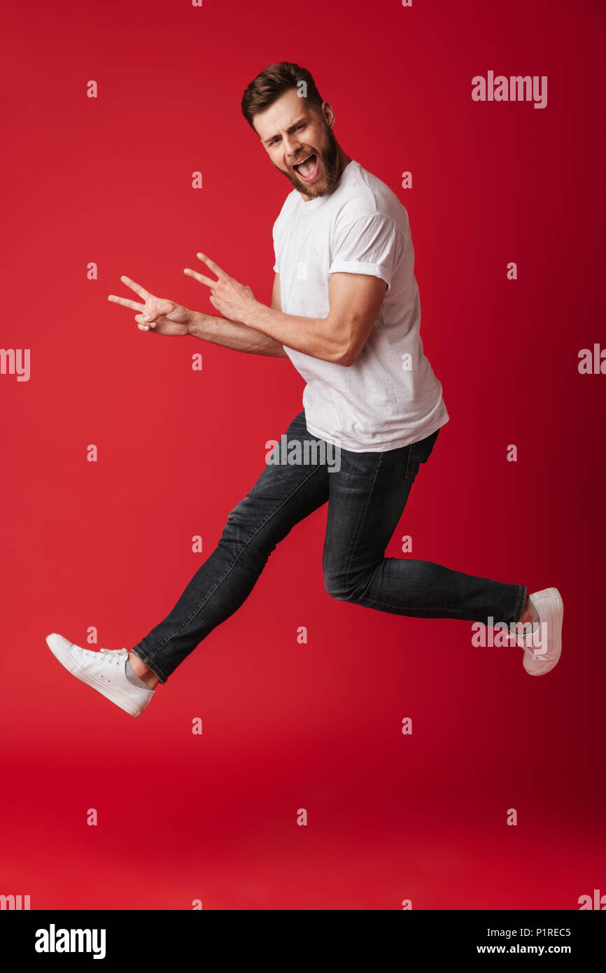 Photo of handsome young man jumping isolated over red wall background ...