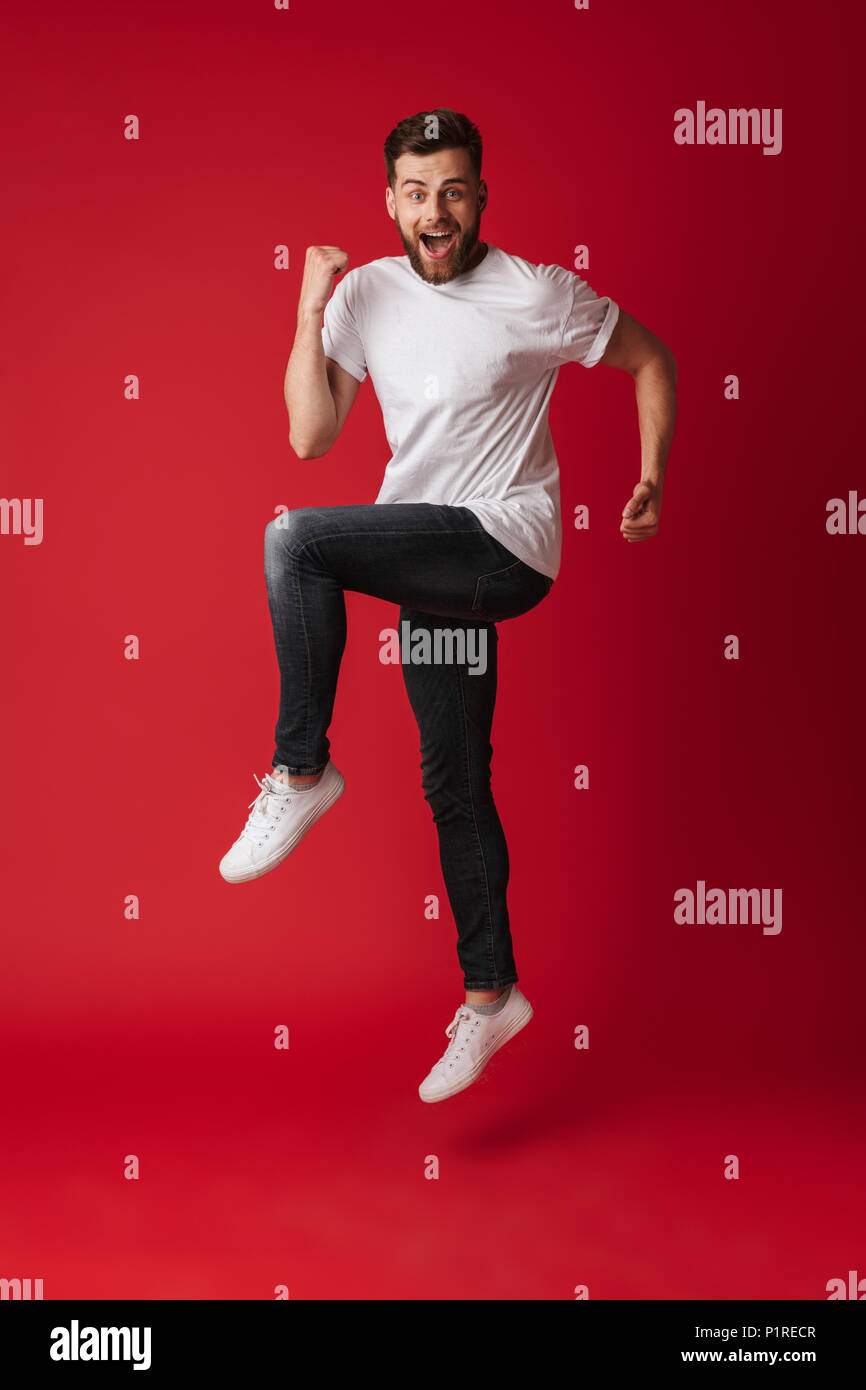 Photo of handsome young man jumping isolated over red wall background ...