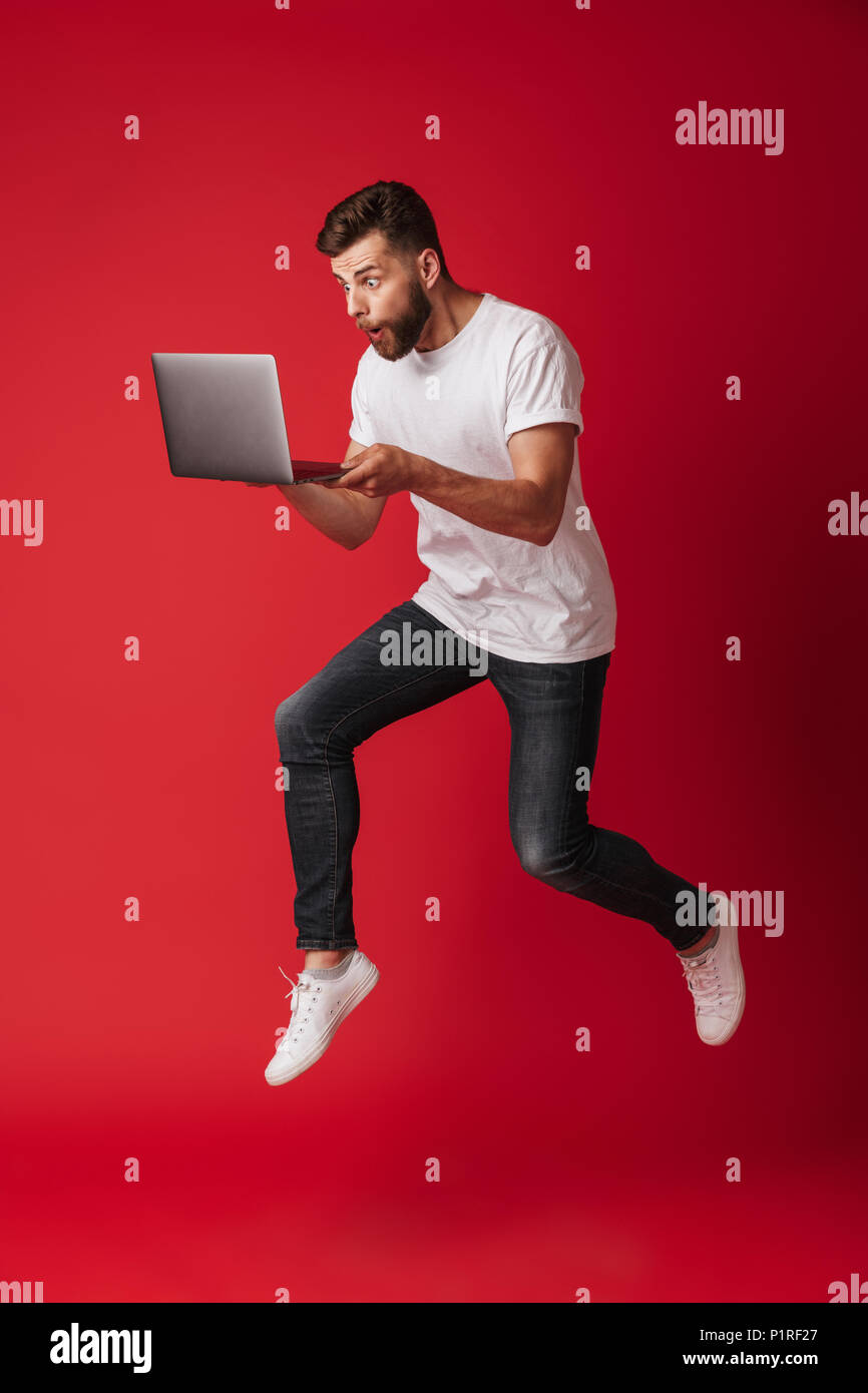 Image of surprised young man jumping isolated over red wall background ...