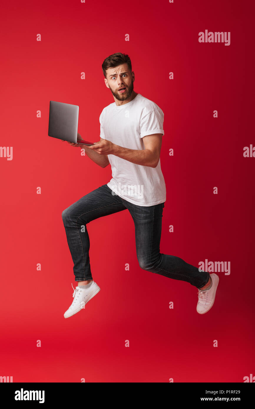 Image of surprised young man jumping isolated over red wall background ...