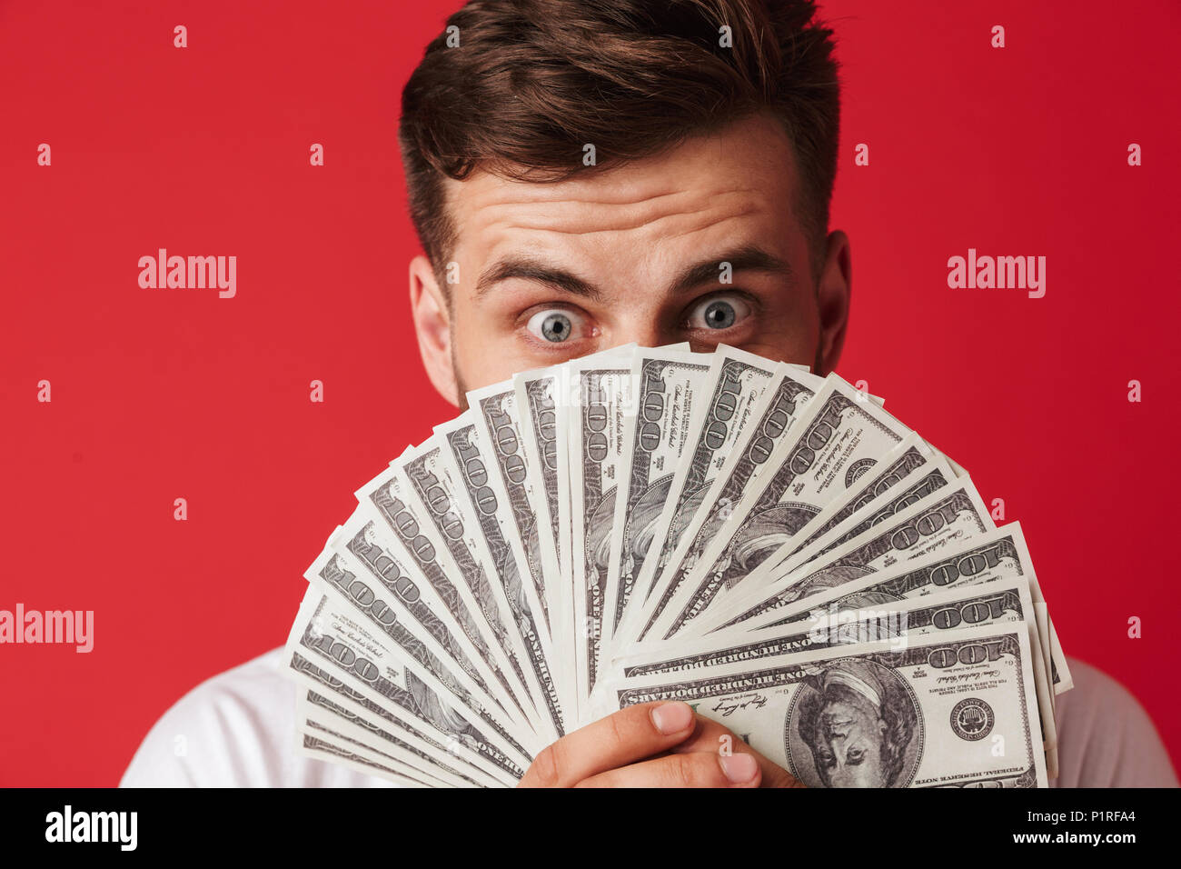 Image of young man isolated over red wall background holding money ...