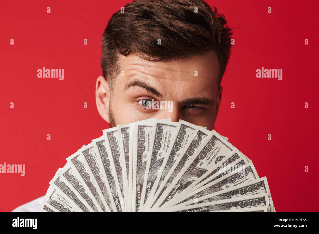Image of young man isolated over red wall background holding money ...