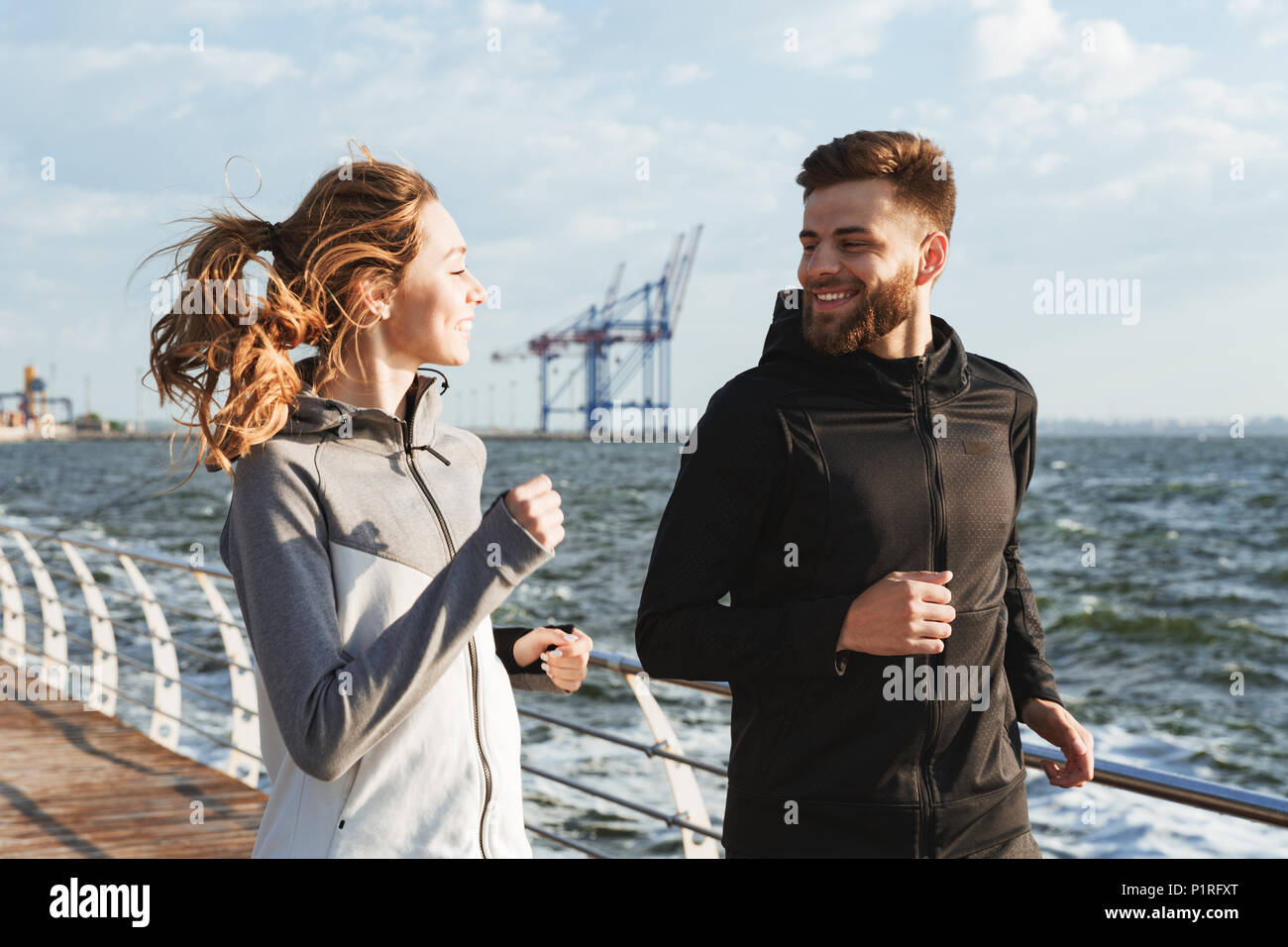 Happy young sports couple talking while jogging together at the beach ...