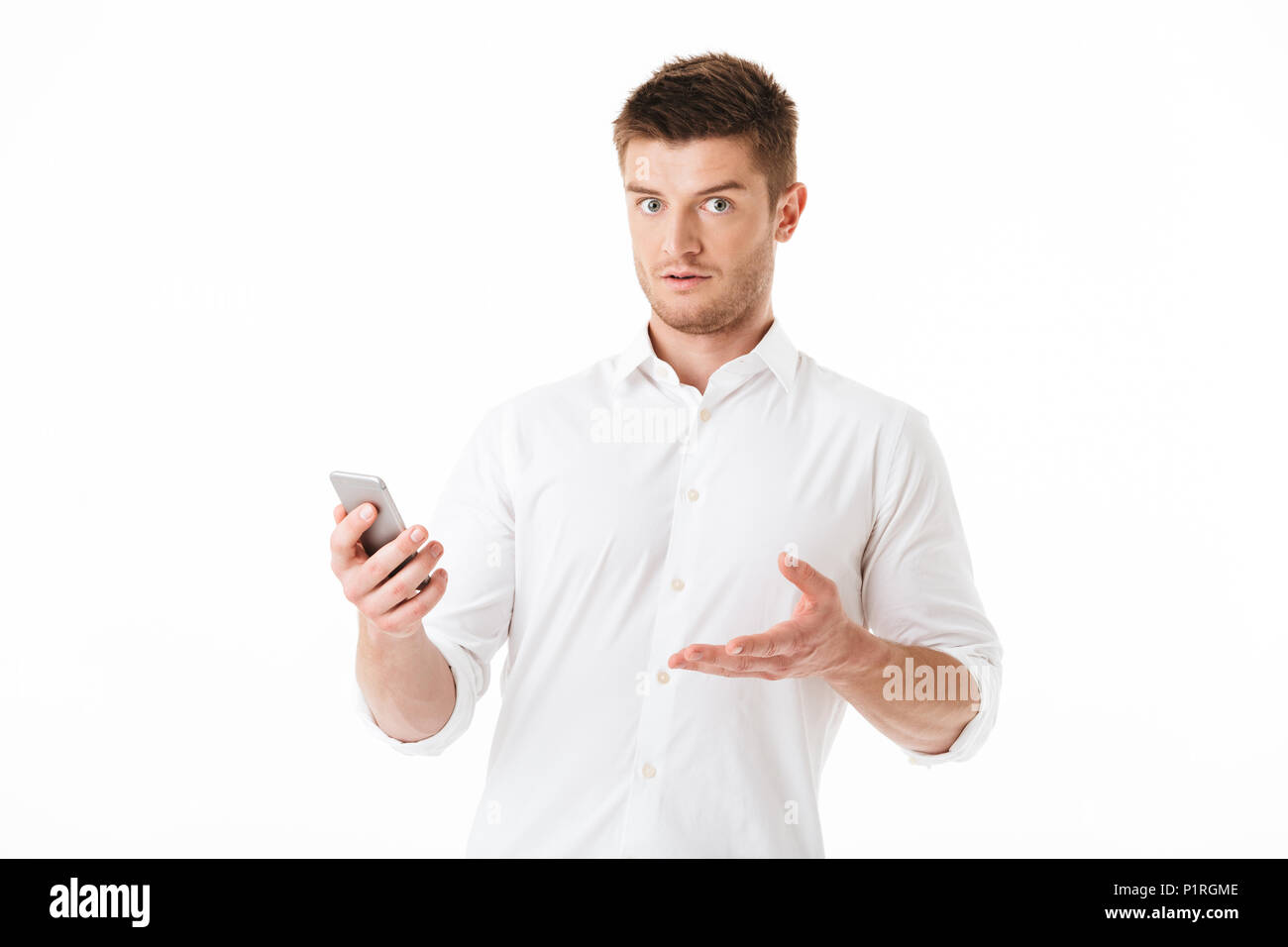 Portrait of a confused young man holding mobile phone isolated over ...