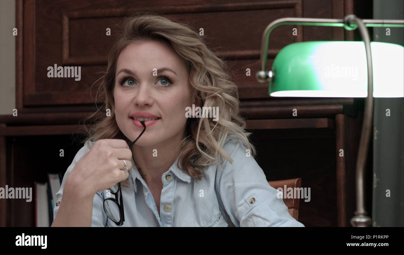 Young female in glasses thinking over her project at desk and suddenly ...