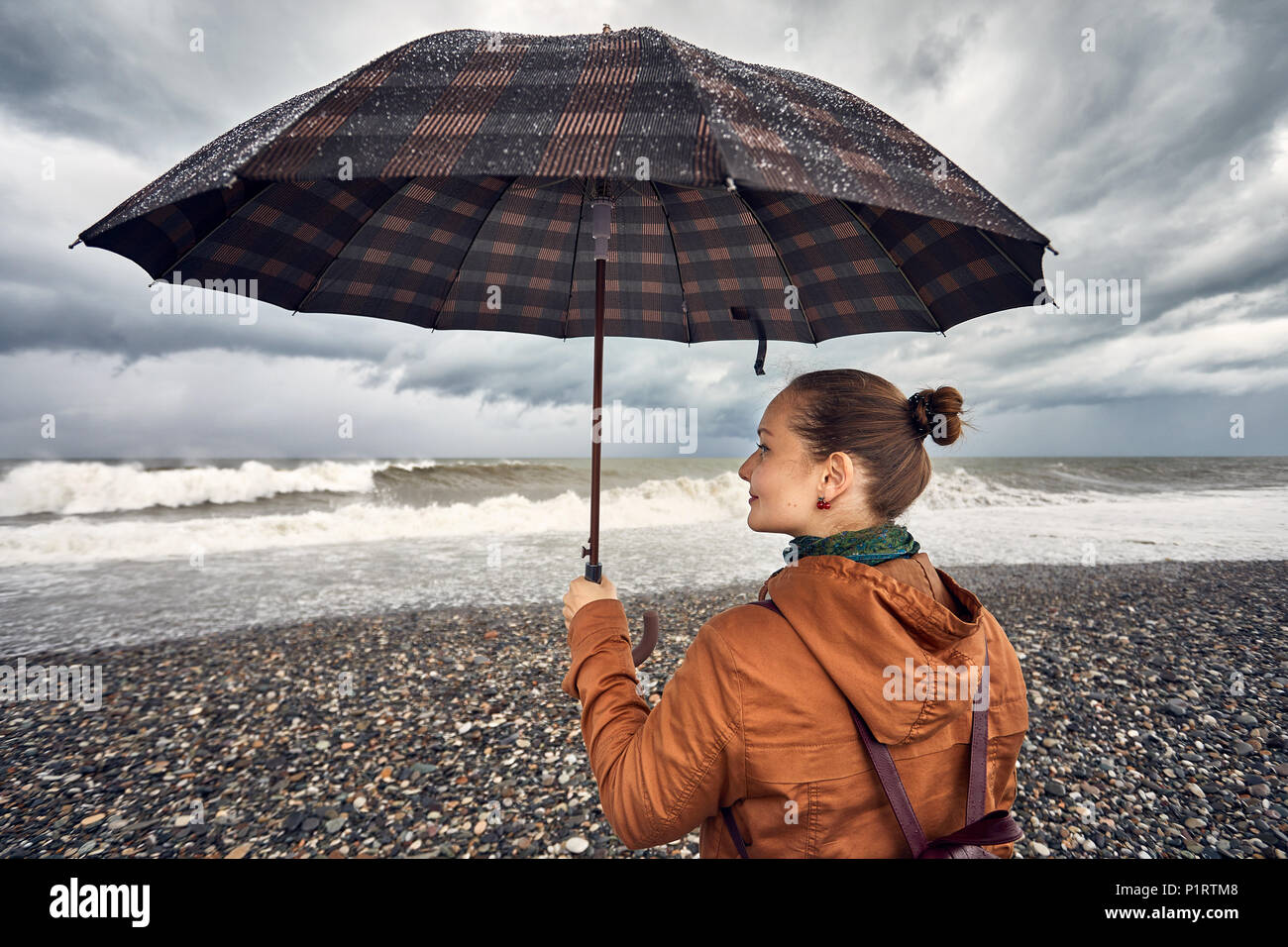 Portrait of beautiful woman with umbrella and backpack looking at ...