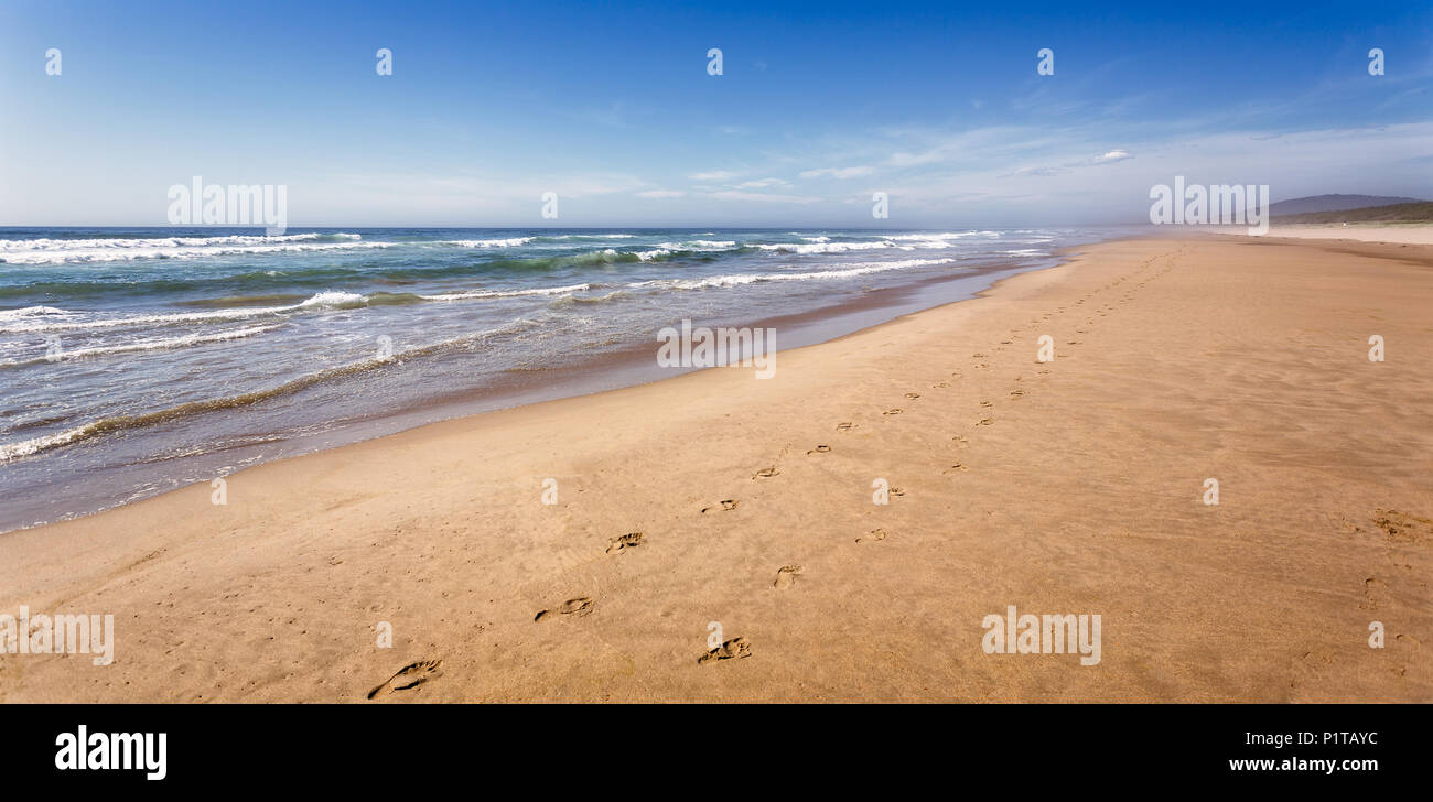 Water lapping on long sandy beach on hot summers day with foorprints ...