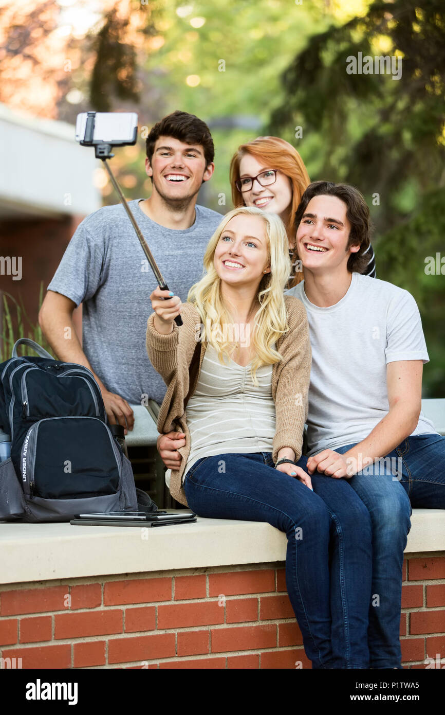 A group of four friends sitting on a bench taking a self-portrait with ...