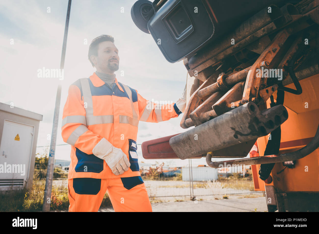 Two refuse collection workers loading garbage into waste truck emptying ...