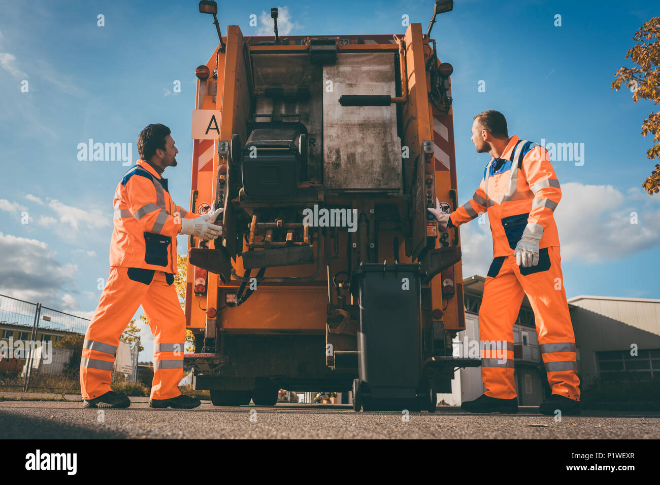 Two refuse collection workers loading garbage into waste truck emptying ...