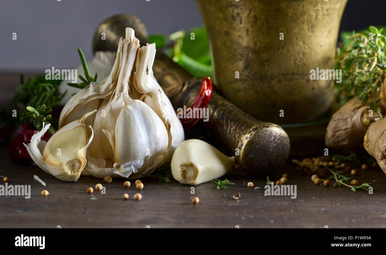 Garlic and different spices on a wooden table . Old copper mortar with ...