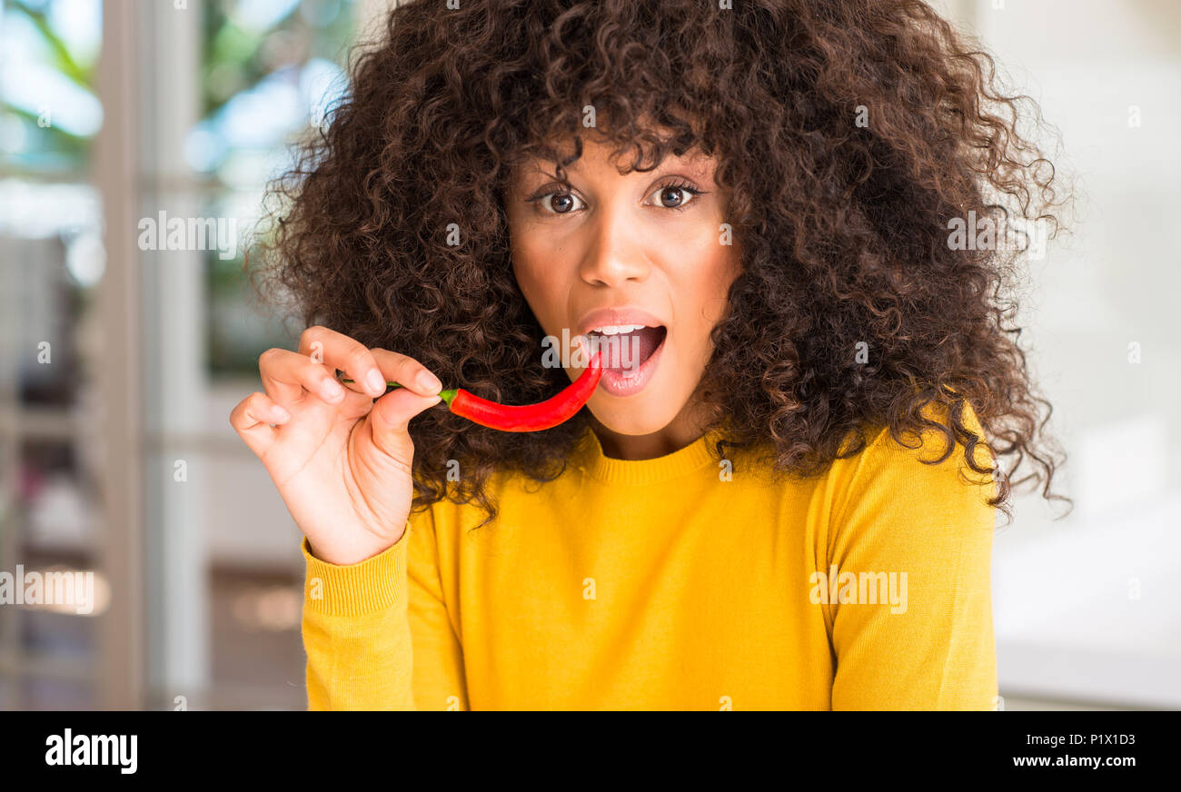 African american woman eating red hot chili pepper scared in shock with ...
