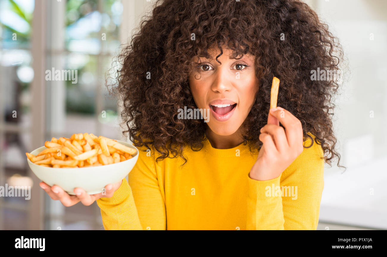 African american woman holding a plate with potato chips at home scared ...