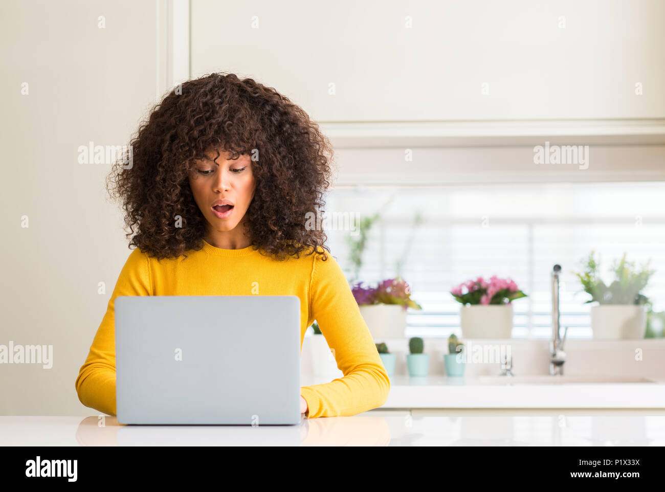 African american woman using computer laptop at kitchen scared in shock ...