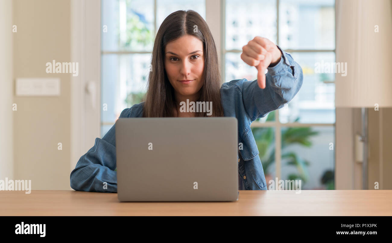 Young woman using laptop at home with angry face, negative sign showing ...