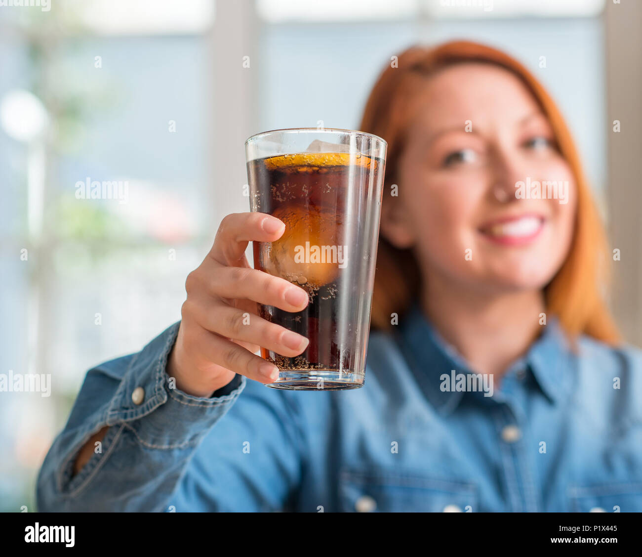 Redhead woman holding soda refreshment with a happy face standing and ...