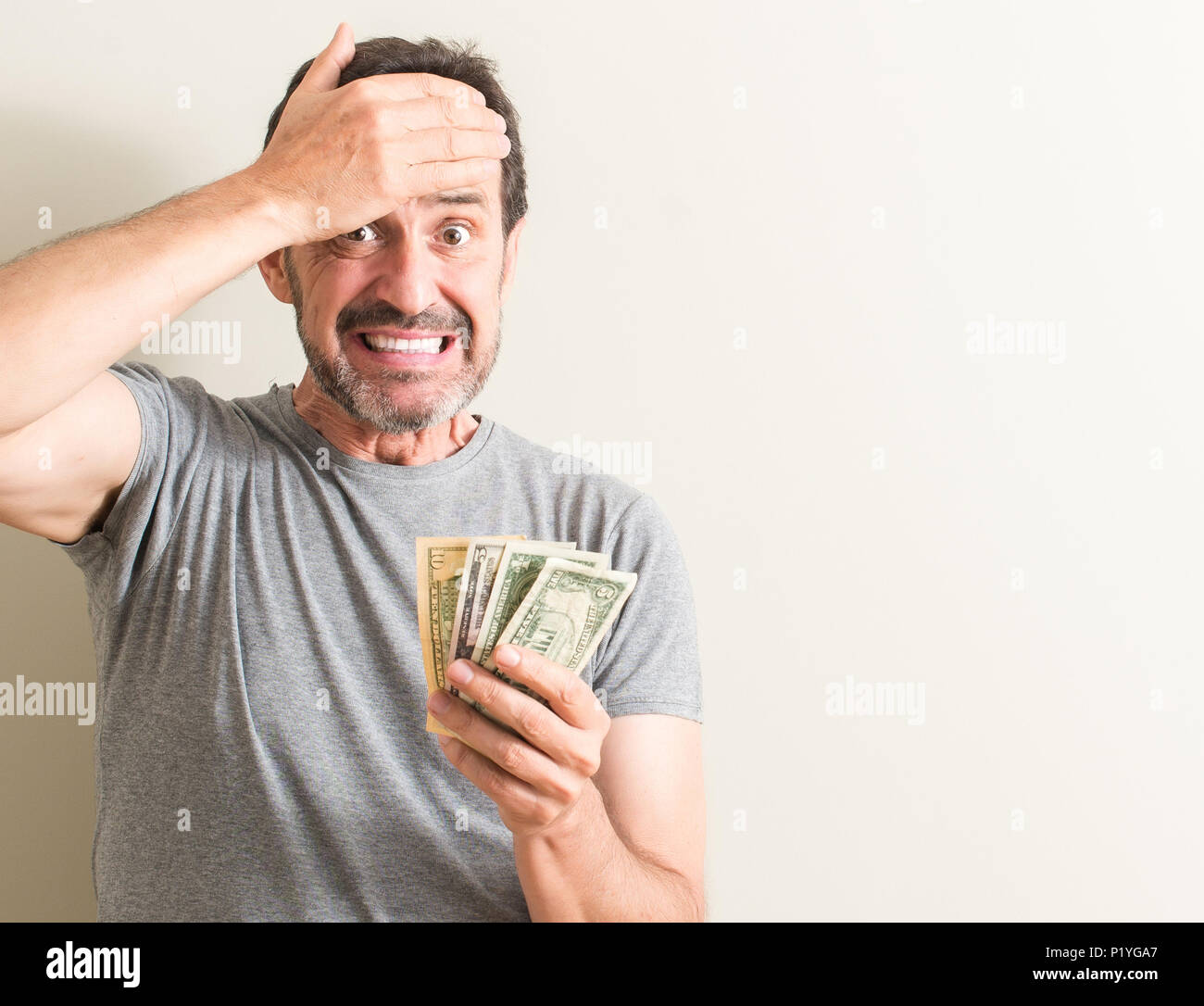 Senior man holding dollar money stressed with hand on head, shocked ...