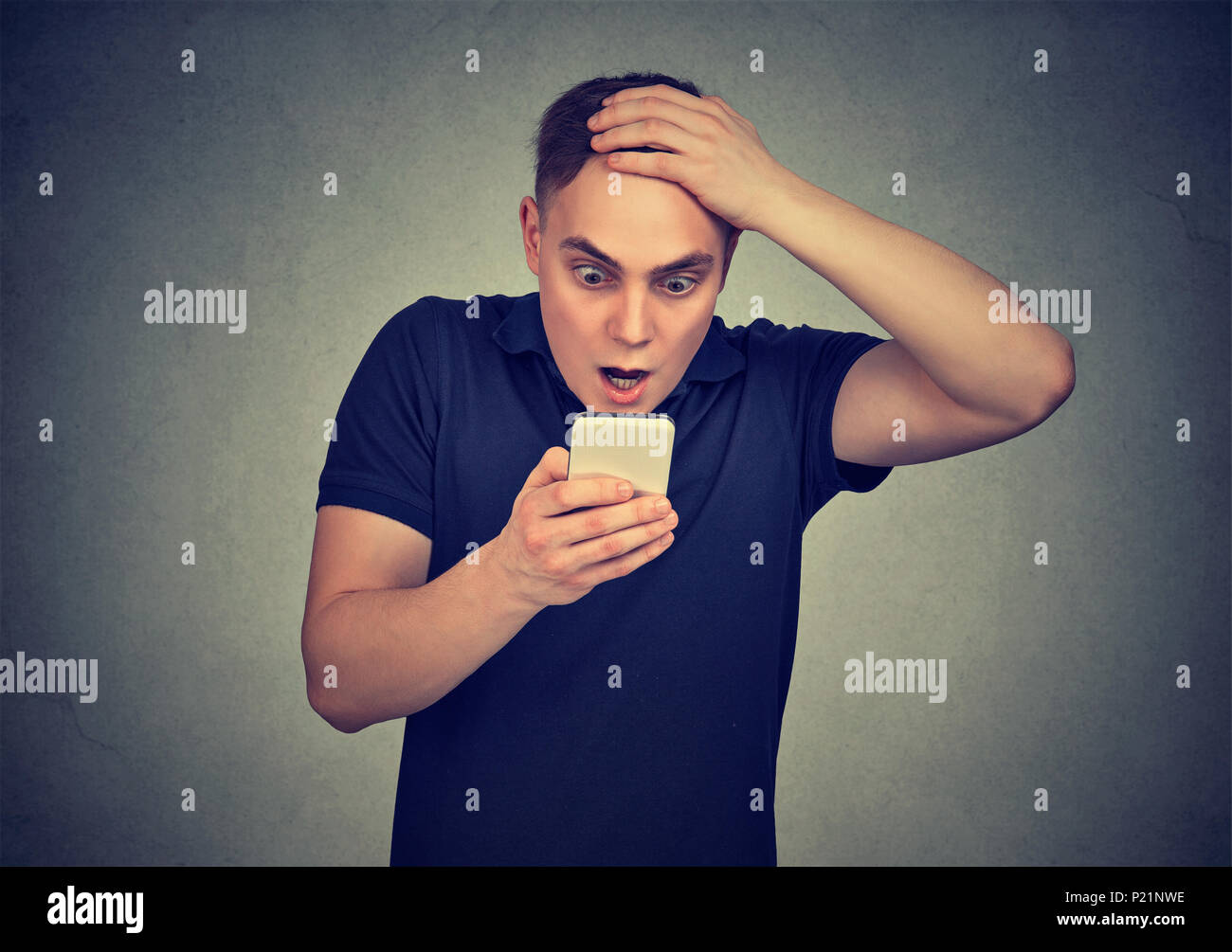 Shocked young man looking at his mobile phone seeing bad news or ...