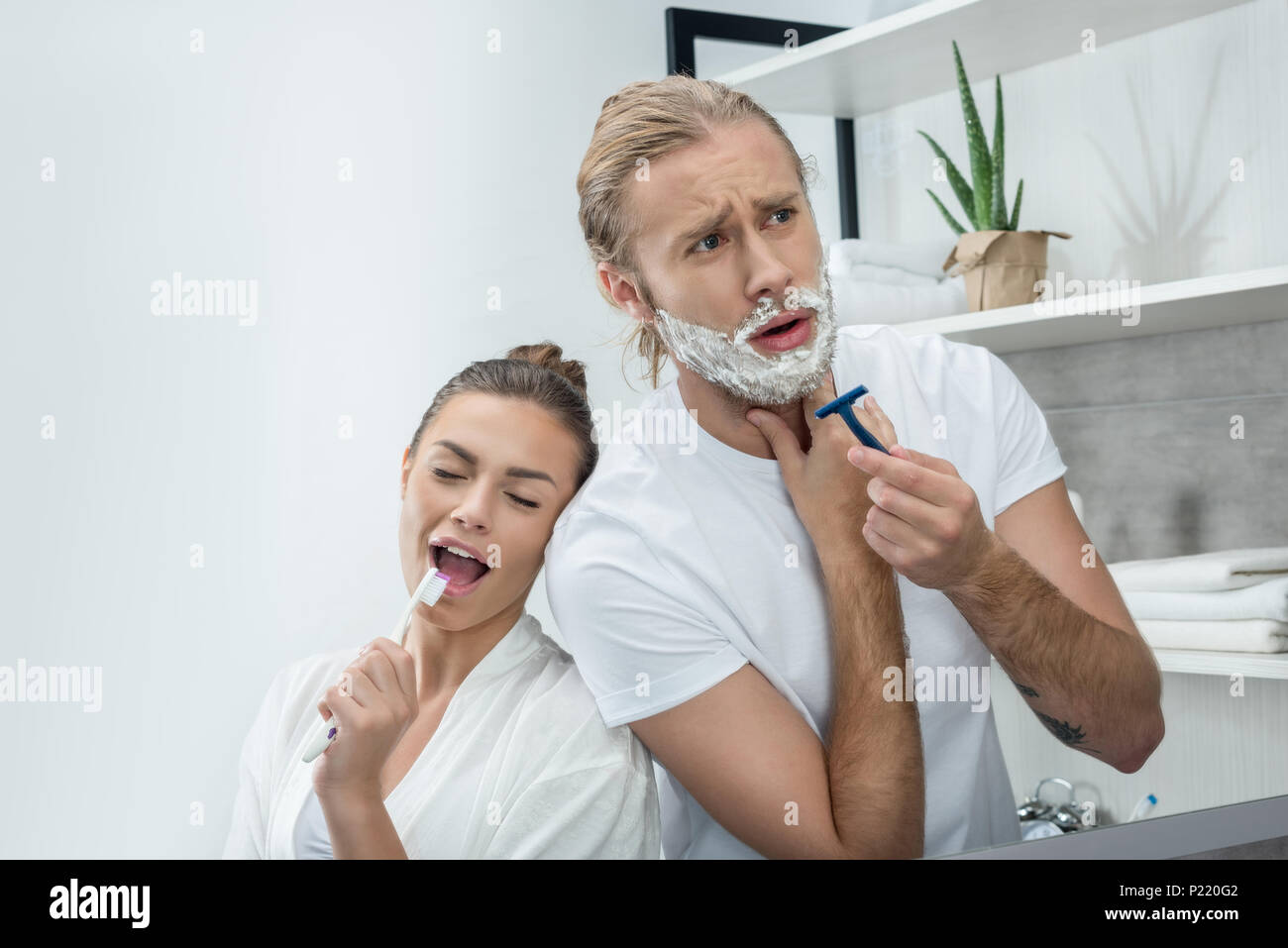 Handsome young man shaving beard with razor while happy woman singing ...