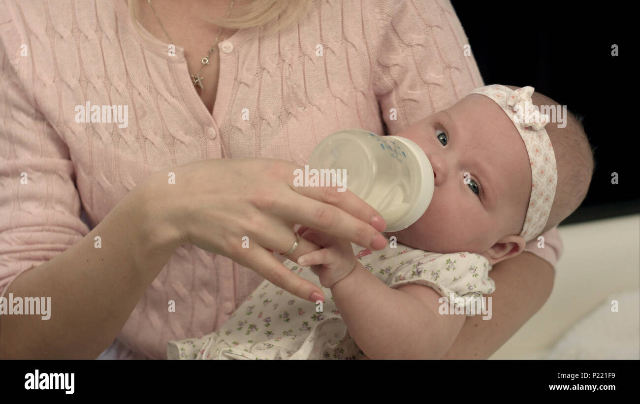 Bright mother feeding milk from bottle her adorable son at home Stock ...