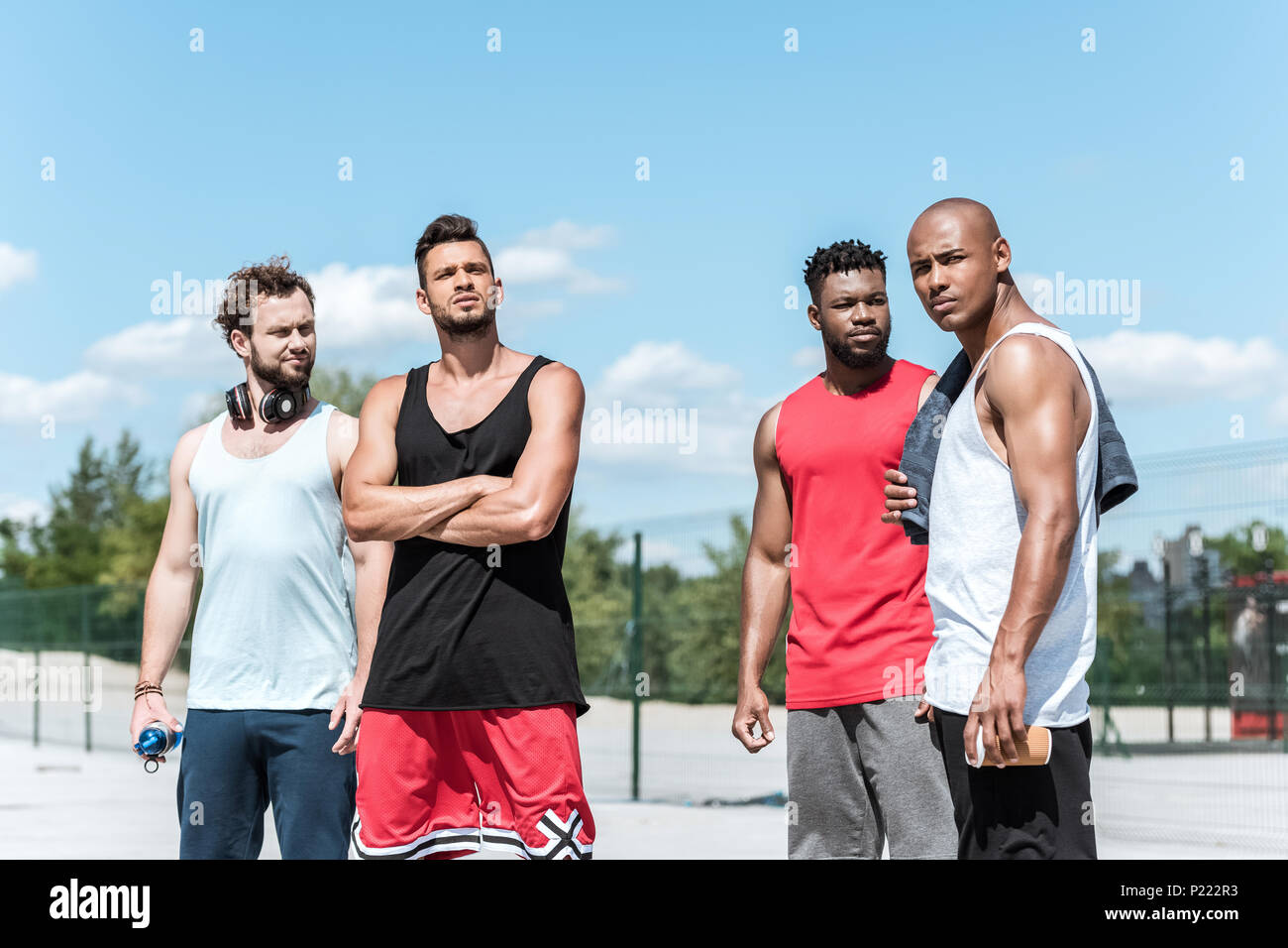 multicultural group of handsome men in sportswear standing on court ...